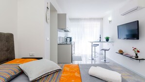 Quarto de hotel moderno com uma cama, uma pequena cozinha, uma TV e um espaço para refeições.