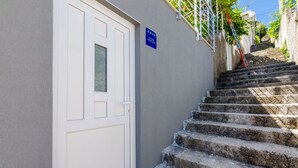 Degraus de pedra levam a uma porta branca com uma placa indicando um apartamento tipo estúdio.