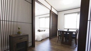 Quarto de hotel com cama, secretária e uma cadeira. Há uma porta de correr e uma janela.