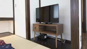 Quarto com uma escrivaninha de madeira, uma televisão em cima e uma cama tipo futon.