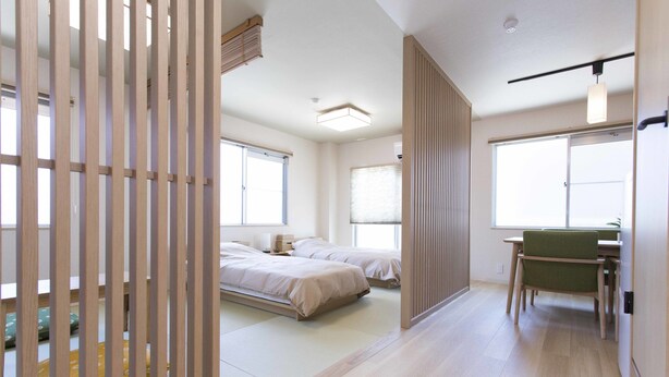 Quarto de hotel moderno com uma cama grande, uma escrivaninha e uma cadeira. Janelas amplas oferecem luz natural.