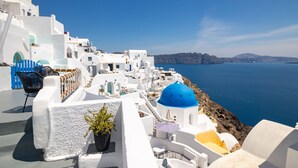 Edifício costeiro com paredes brancas e cúpulas azuis, com vista para um mar azul e límpido.