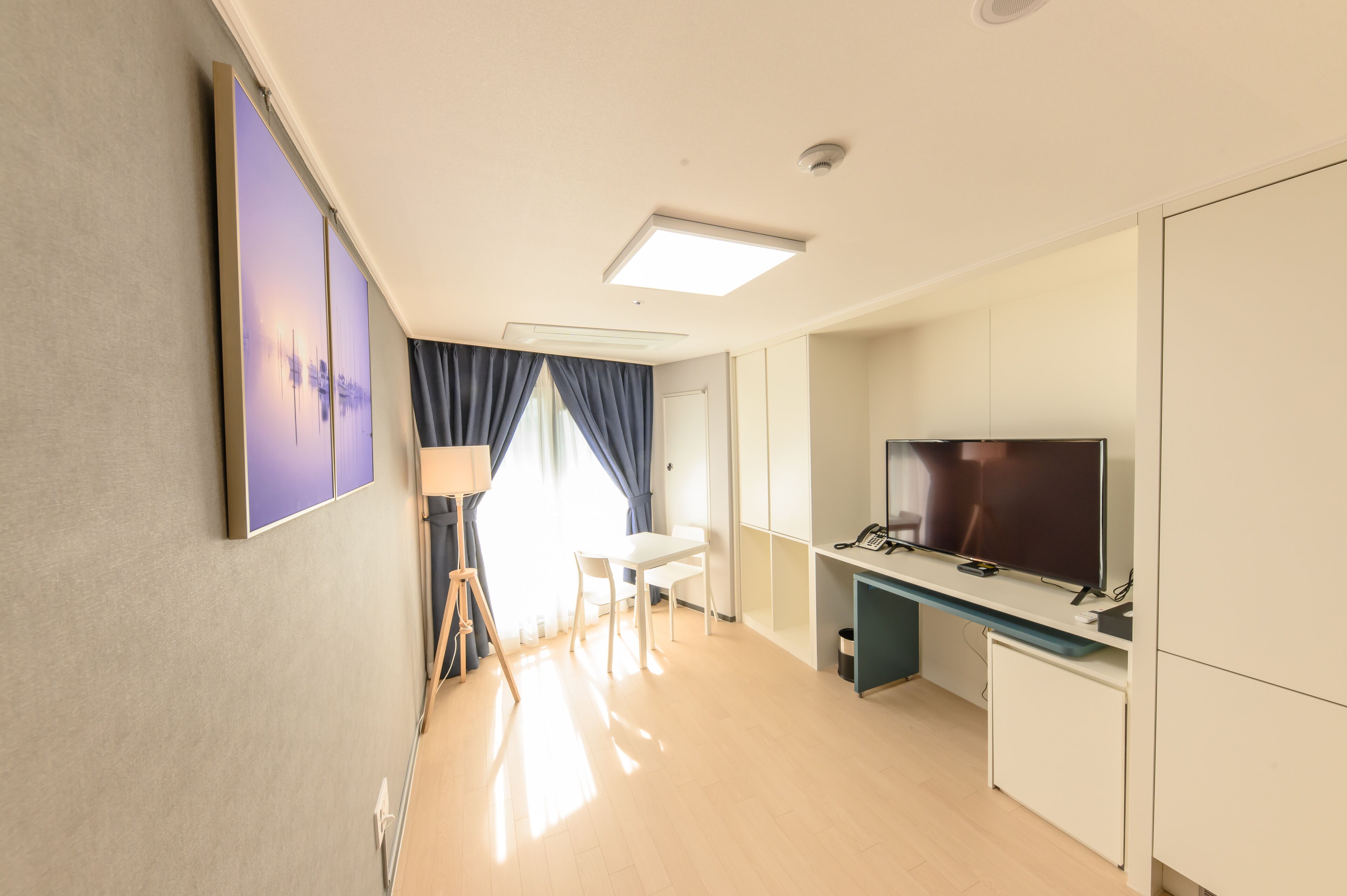 Quarto de hotel moderno com televisão de ecrã plano, secretária, cadeira e uma grande janela com cortinas.