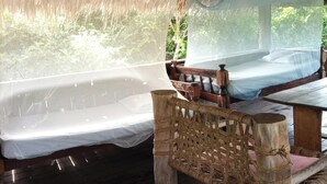 Uma cama de madeira rústica com mosquiteiro, um banco trançado e uma estrutura de telhado de palha.