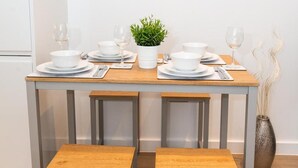 Uma sala de jantar com uma mesa posta para quatro pessoas, uma planta em vaso e um vaso com plantas secas.