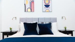 Quarto de hotel moderno com uma cama grande, duas mesas de cabeceira e arte abstrata nas paredes.