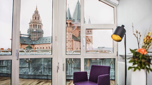 Quarto com uma grande janela que oferece vista para um edifício histórico com torre de relógio.