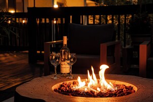 Uma mesa de madeira com uma garrafa de vinho, duas taças e uma lareira acesa.