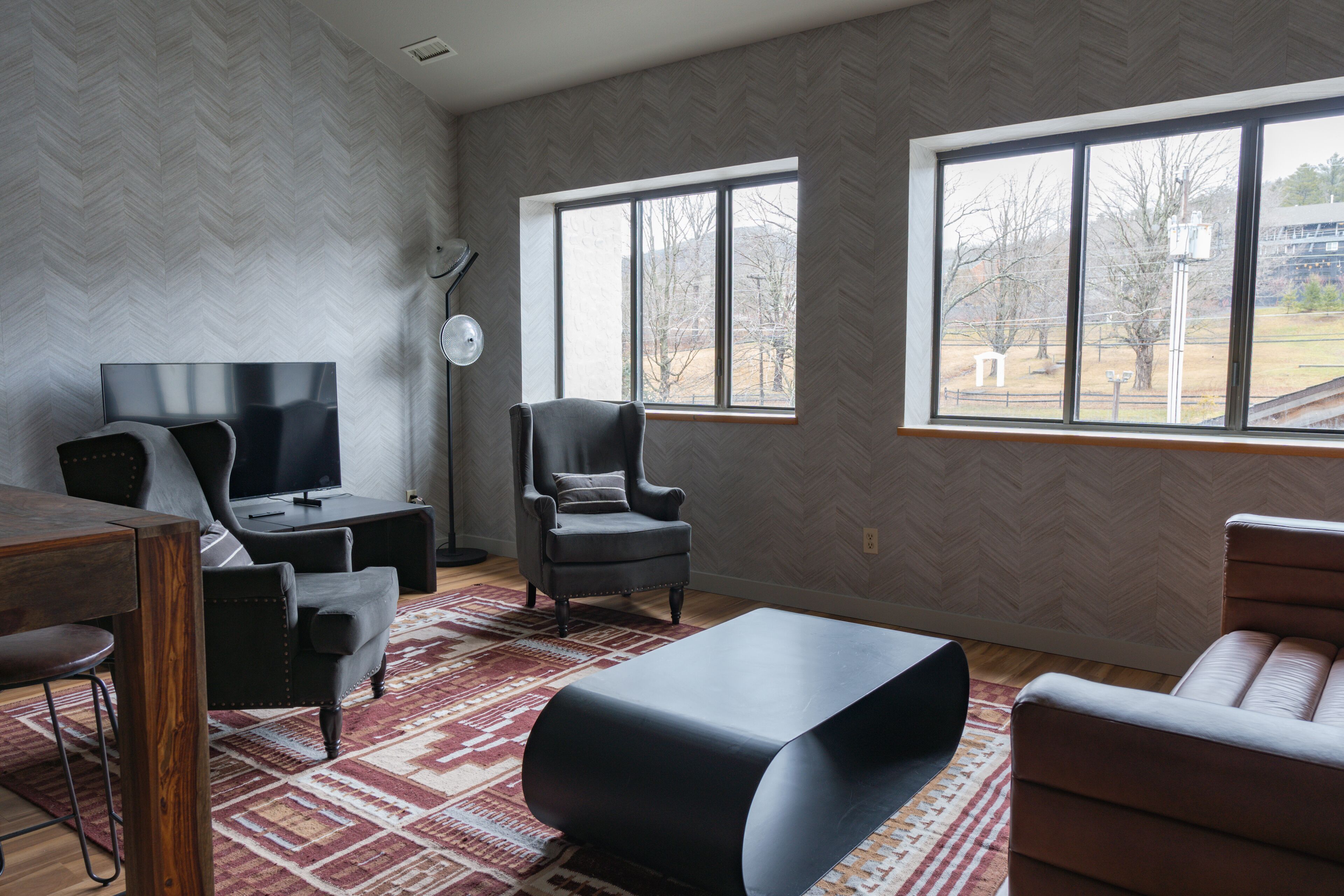 Uma sala de estar moderna com uma TV de tela plana, sofás de couro, uma mesa de centro e grandes janelas com vista para o exterior.