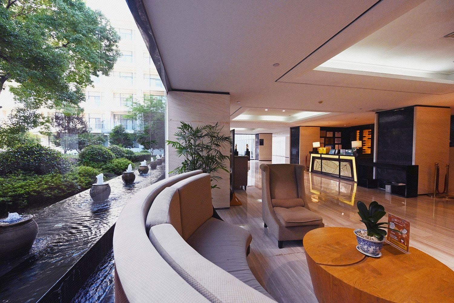 Um lobby moderno com área de estar em curva, balcão de recepção e vista para um espelho d'água ao ar livre.