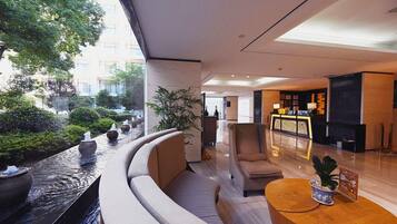 Um lobby moderno com área de estar em curva, balcão de recepção e vista para um espelho d'água ao ar livre.