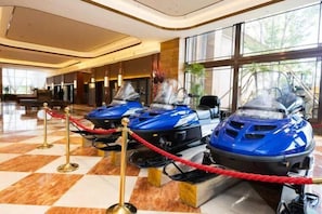 Um hall com piso xadrez, um balcão de recepção e três veículos de neve azuis em exposição.