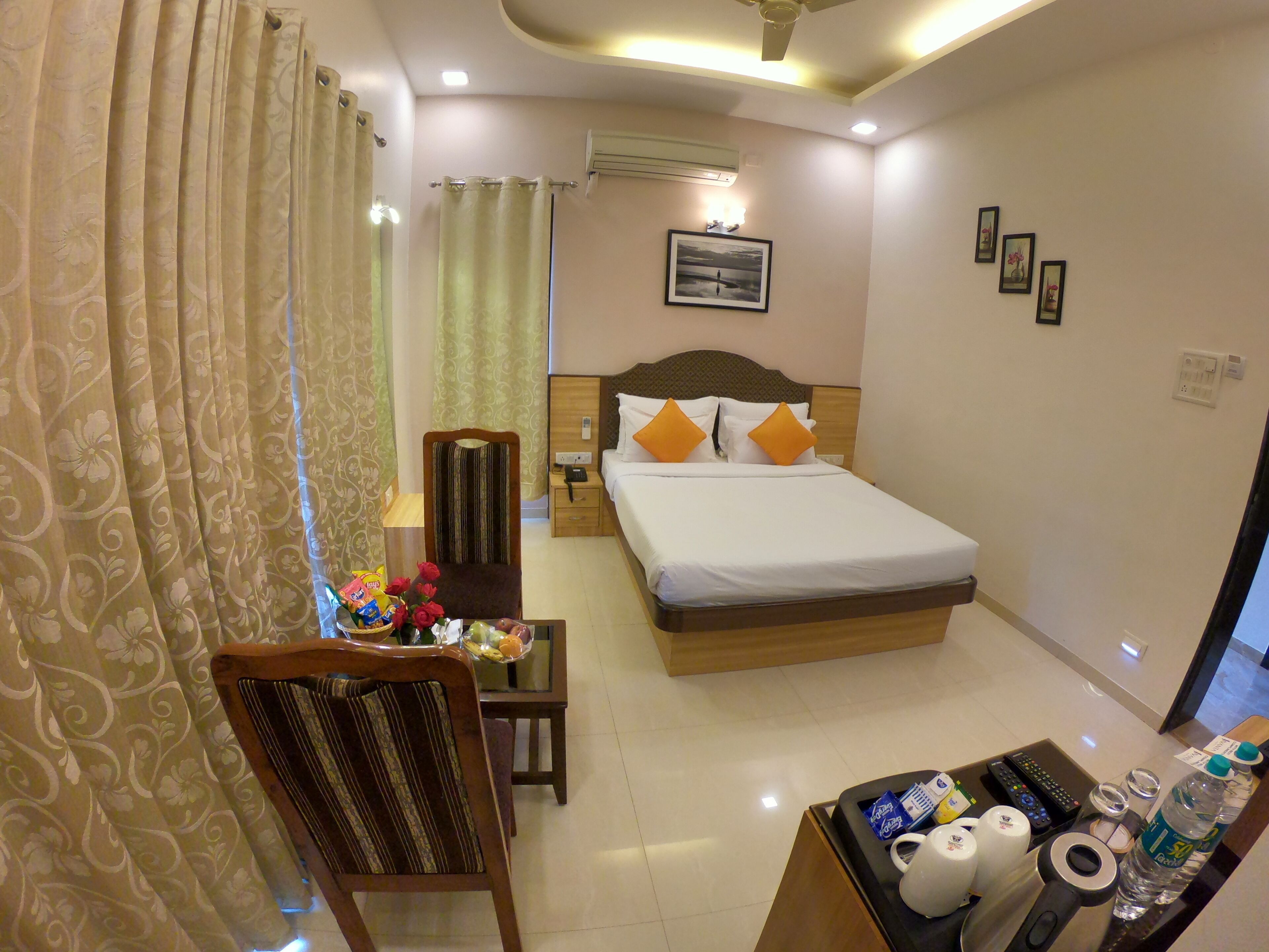 Quarto de hotel com uma cama, uma escrivaninha com cadeira, uma mesa com um vaso de flores e uma mesa de cabeceira com abajur.
