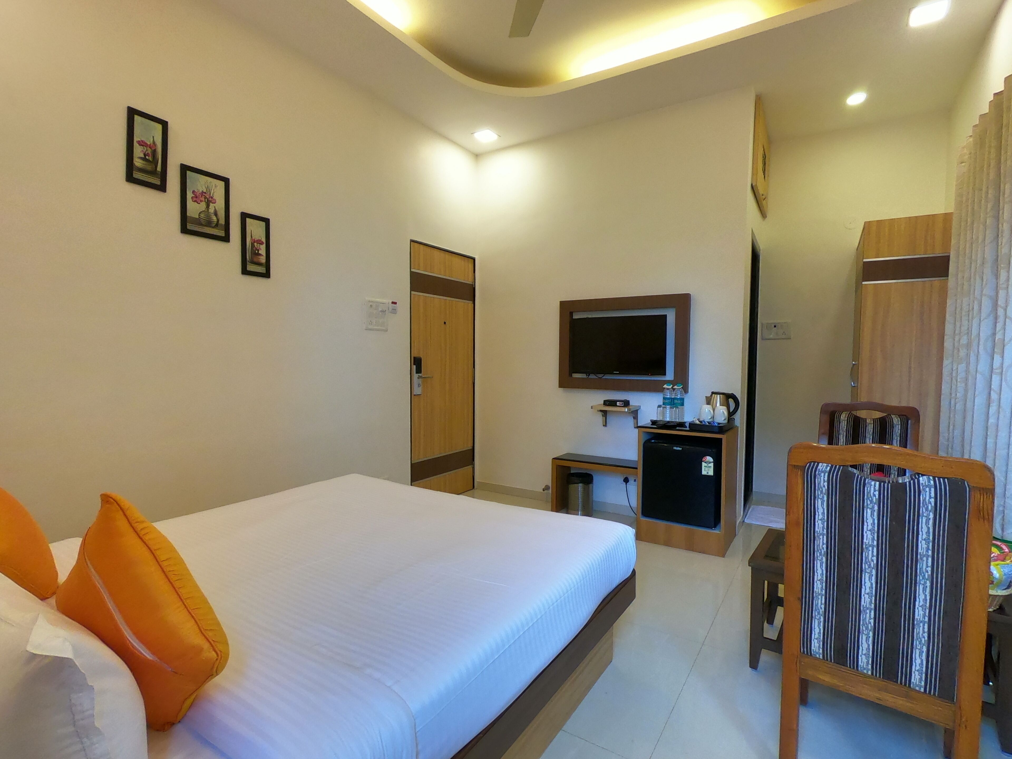 Quarto de hotel com uma cama, uma escrivaninha com televisão, um frigorífico e uma cadeira.