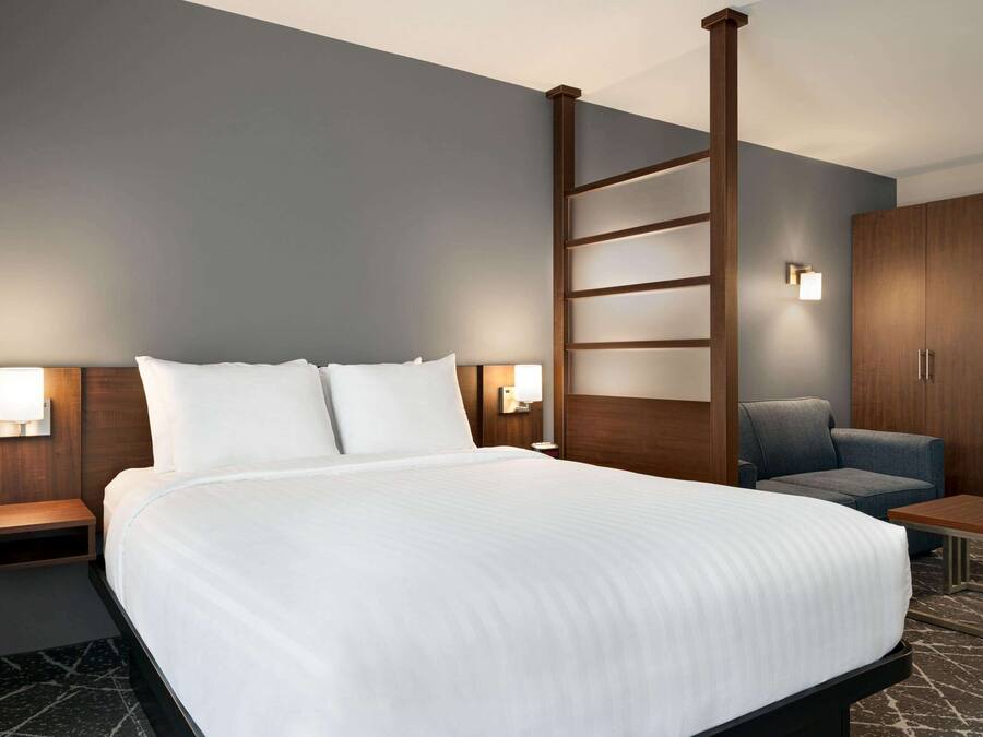 Quarto de hotel com uma cama grande, uma mesa de cabeceira, uma escrivaninha, uma cadeira e um guarda-roupa.