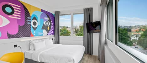 Quarto de hotel moderno com uma cama, uma escrivaninha, uma cadeira, uma televisão e uma grande janela com vista para a cidade.