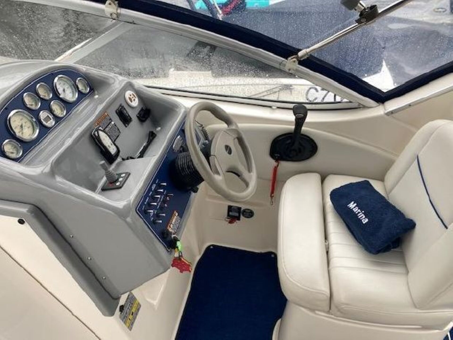 Interior de barco com leme, painel de controle e área de estar.