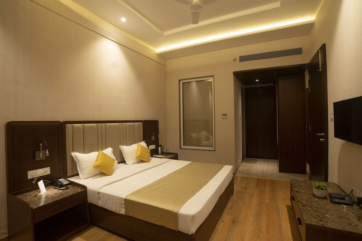 Quarto de hotel com cama, mesa de cabeceira, televisão e escrivaninha com uma planta.