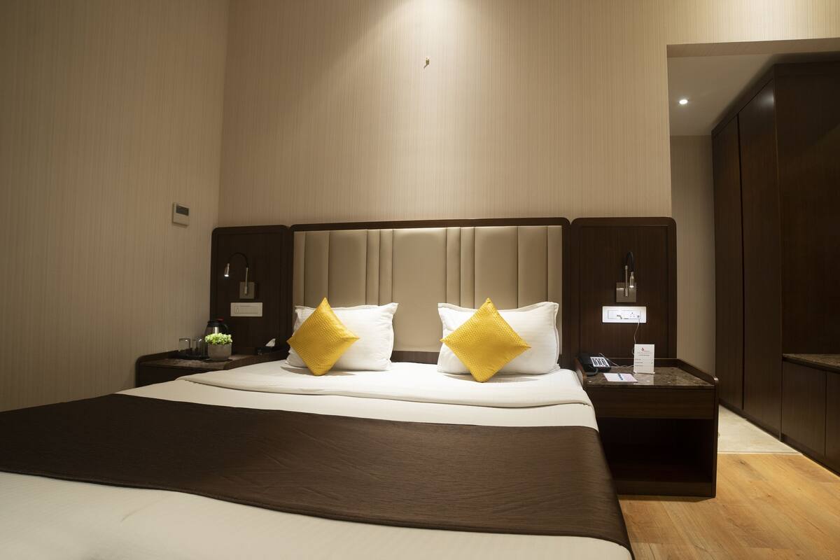 Quarto de hotel com uma cama grande, duas mesas de cabeceira, um criado-mudo, um espelho e um guarda-roupa.