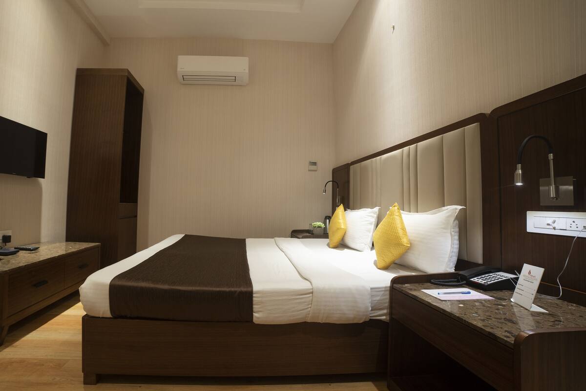 Quarto de hotel com cama, mesa de cabeceira, escrivaninha e televisão de tela plana na parede.