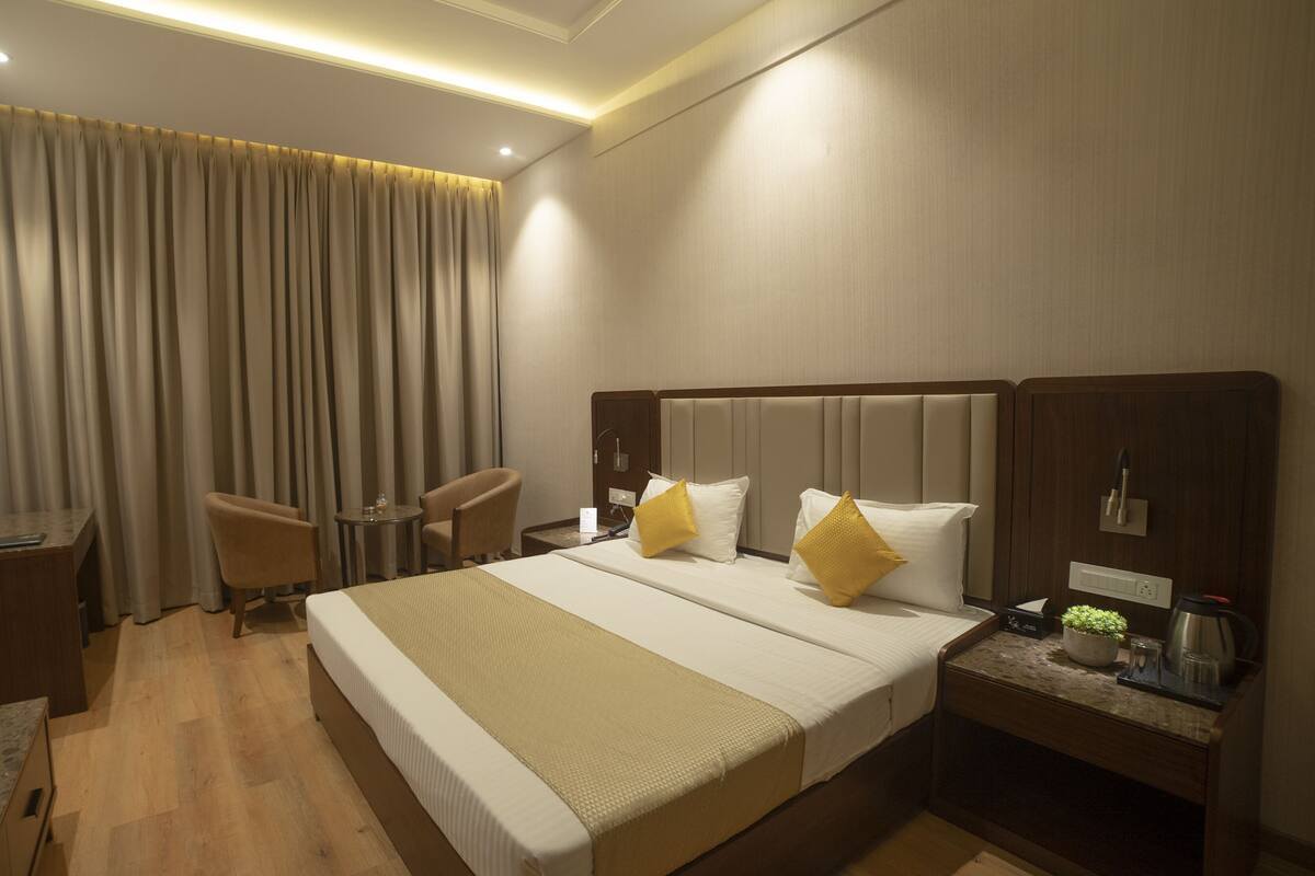 Quarto de hotel com cama, mesa de cabeceira, cadeira e uma pequena mesa com abajur.