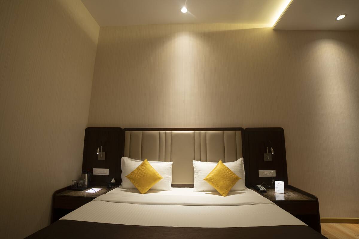Quarto de hotel com cama grande, duas mesas de cabeceira e cabeceira moderna.