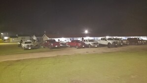 Estacionamento à noite com vários veículos estacionados.