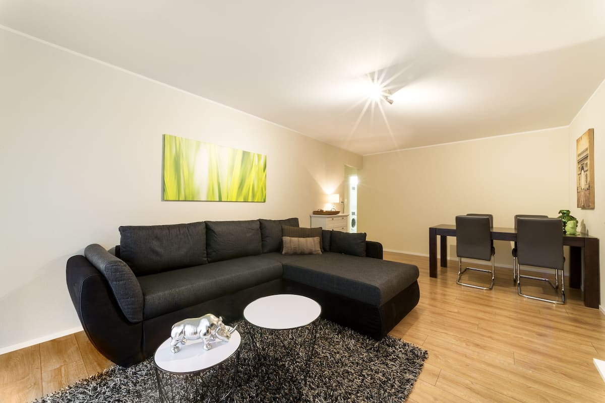 Uma sala de estar moderna com um sofá seccional, uma mesa de centro redonda e um espaço de jantar com duas cadeiras e uma mesa.