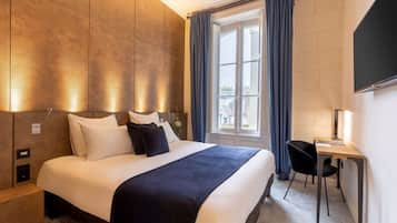 Quarto de hotel moderno com uma cama grande, uma escrivaninha e uma janela com cortinas.