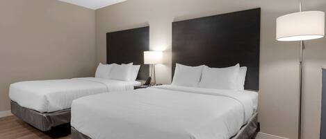 Quarto de hotel com duas camas, uma mesa de cabeceira com abajur e um candeeiro de chão.
