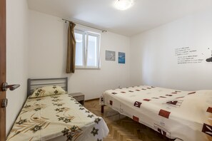 Quarto com duas camas de solteiro, janela com cortinas, luminária na parede e uma pequena mesa de cabeceira.