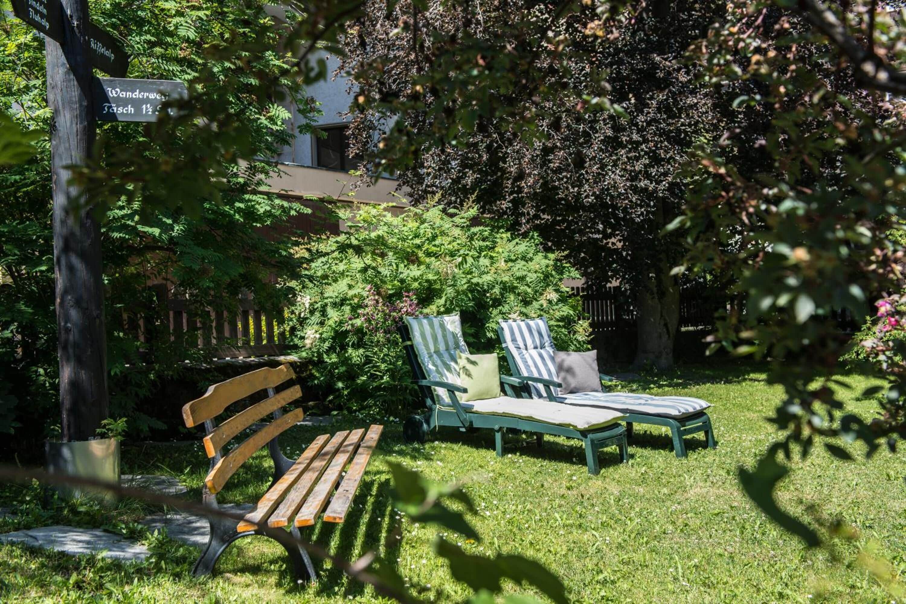 Um jardim com um banco de madeira e duas cadeiras de descanso listradas.