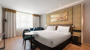 Quarto de hotel moderno com uma cama grande, uma escrivaninha, uma cadeira e uma mesinha.