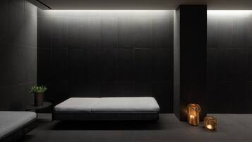 Quarto moderno e com iluminação suave, design minimalista, com uma cama de solteiro, uma mesinha com uma planta e duas luminárias que lembram velas.