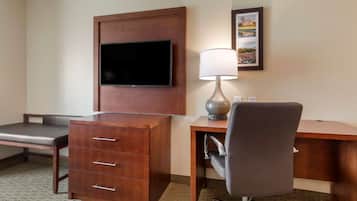 Quarto de hotel com escrivaninha de madeira, uma cadeira, televisão fixada na parede, abajur e quadro emoldurado.
