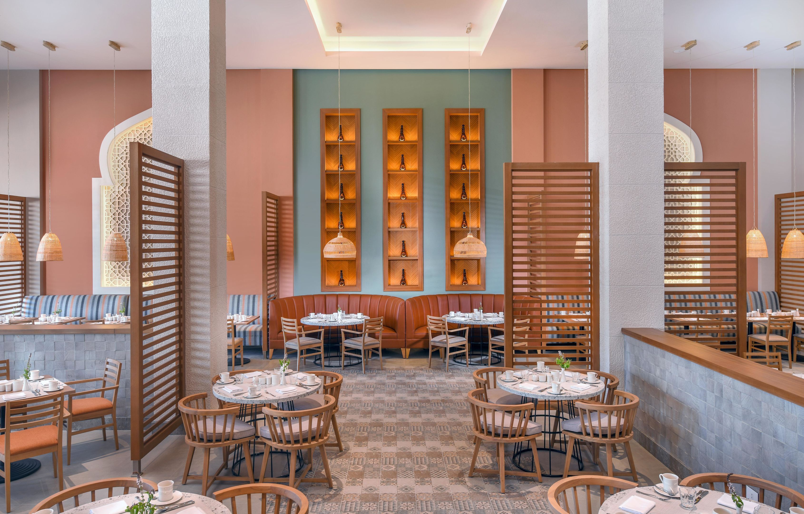 Um restaurante com mesas redondas, cabines acolchoadas e luminárias pendentes.