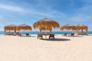 Uma praia com guarda-sóis de palha, espreguiçadeiras e vista para o mar.
