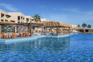 Uma área à beira da piscina com bar, espreguiçadeiras e uma estrutura de telhado de palha.