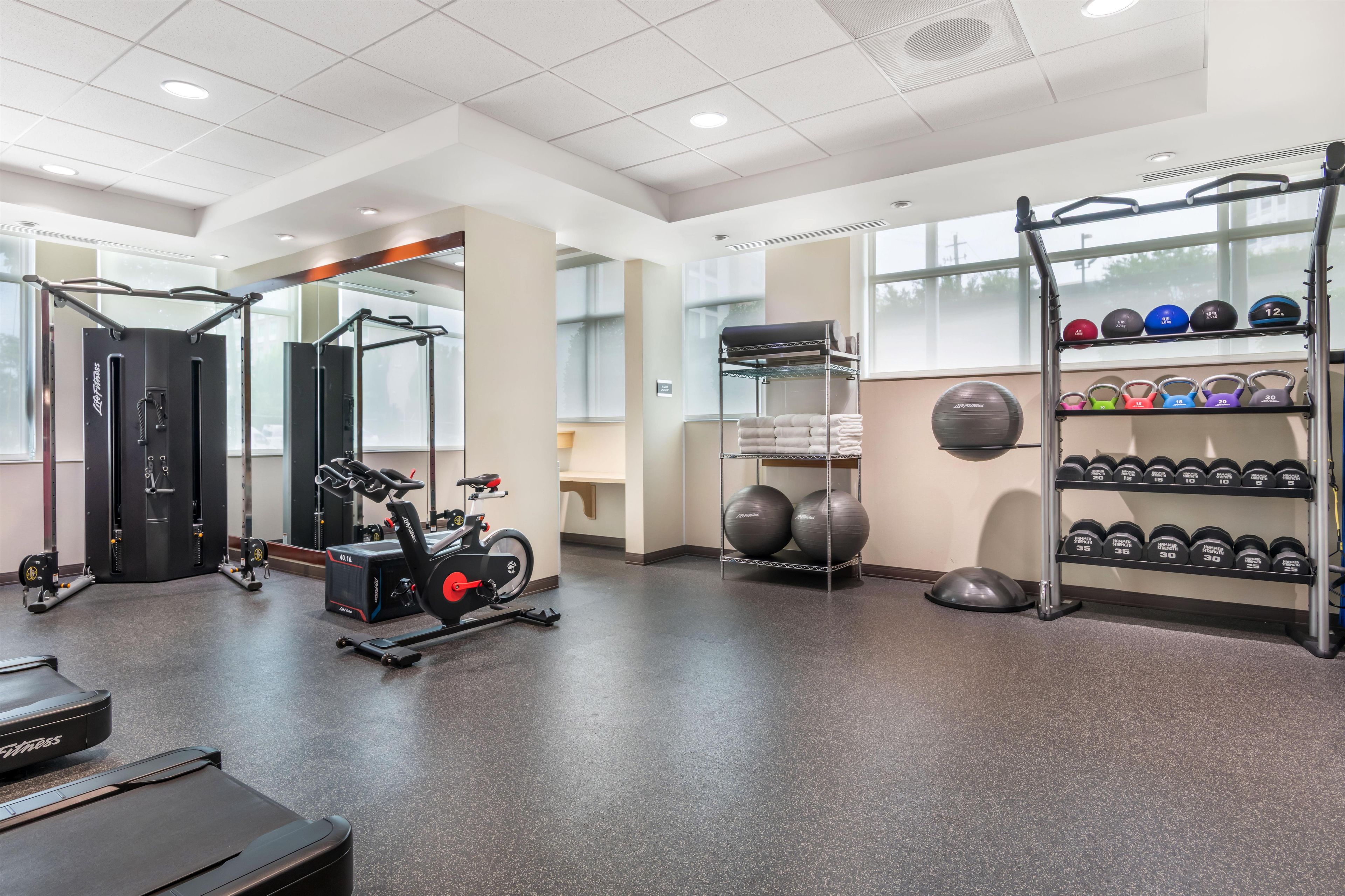 Uma academia com equipamentos de exercícios, incluindo uma máquina de remo, barra de puxada e um suporte com halteres.