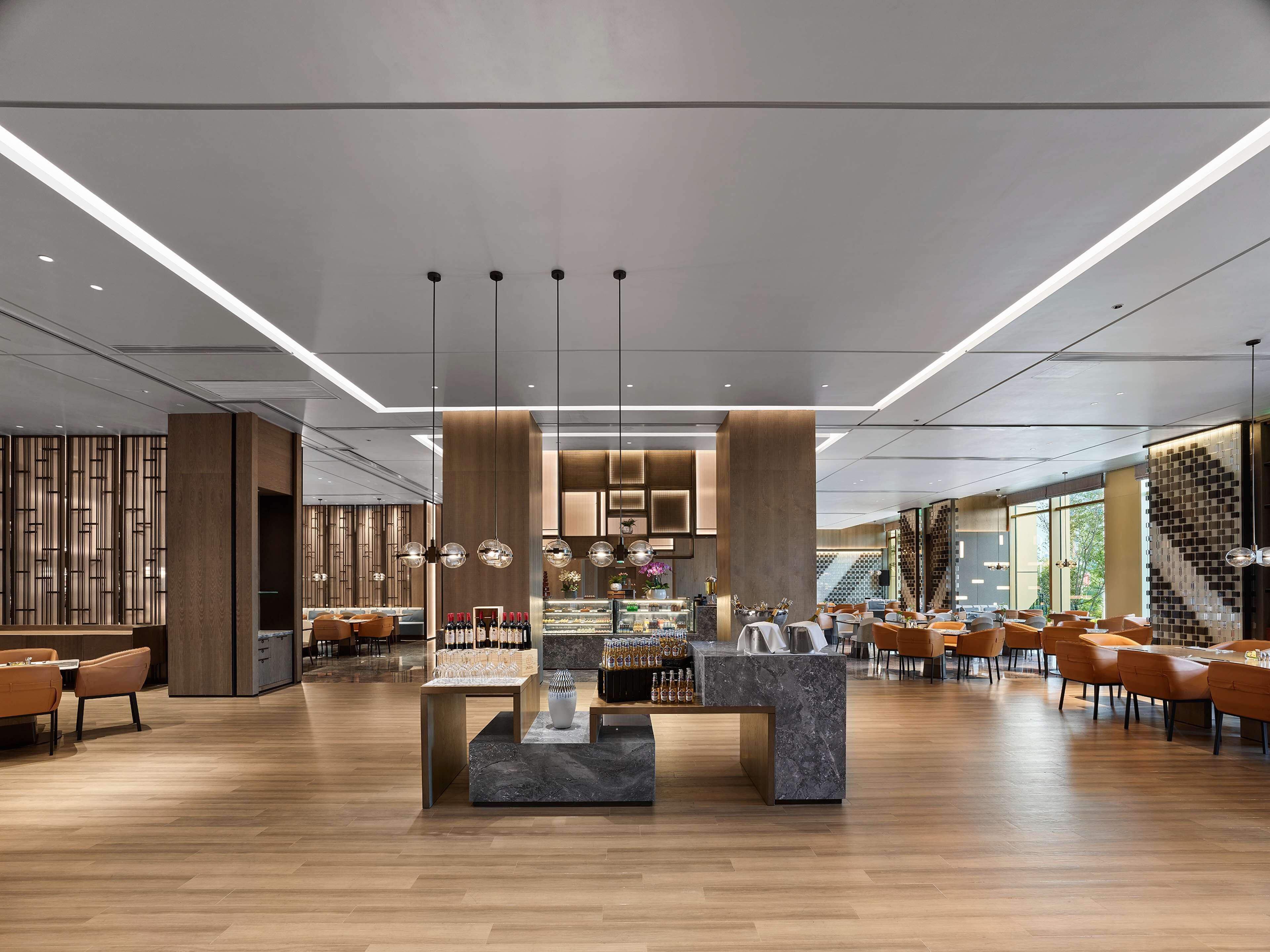 Um lobby de hotel moderno com área de bar central, espaços de estar e vista para o exterior.