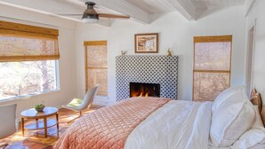 Quarto com cama, lareira, poltrona e janela com persianas.