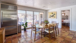 Uma cozinha moderna com geladeira de aço inoxidável, uma mesa de jantar com cadeiras e janelas amplas com vista para o exterior.