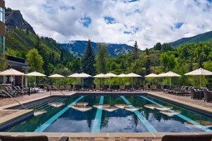 Piscina com espreguiçadeiras e guarda-sóis, rodeada por montanhas e árvores.