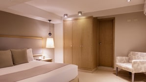 Quarto com uma cama grande, um guarda-roupa de madeira, uma cadeira e uma mesa de cabeceira com abajur.