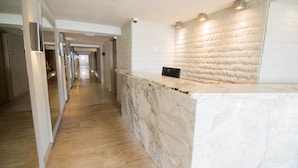 Uma área de recepção de hotel com balcão de mármore, um computador e uma parede de pedra.