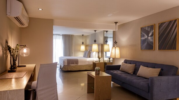 Quarto de hotel moderno com cama, sofá, escrivaninha e luminária.