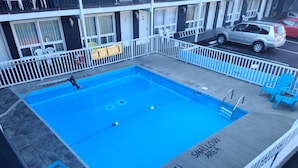 Piscina com área rasa demarcada, cercada por um muro branco e cadeiras azuis.