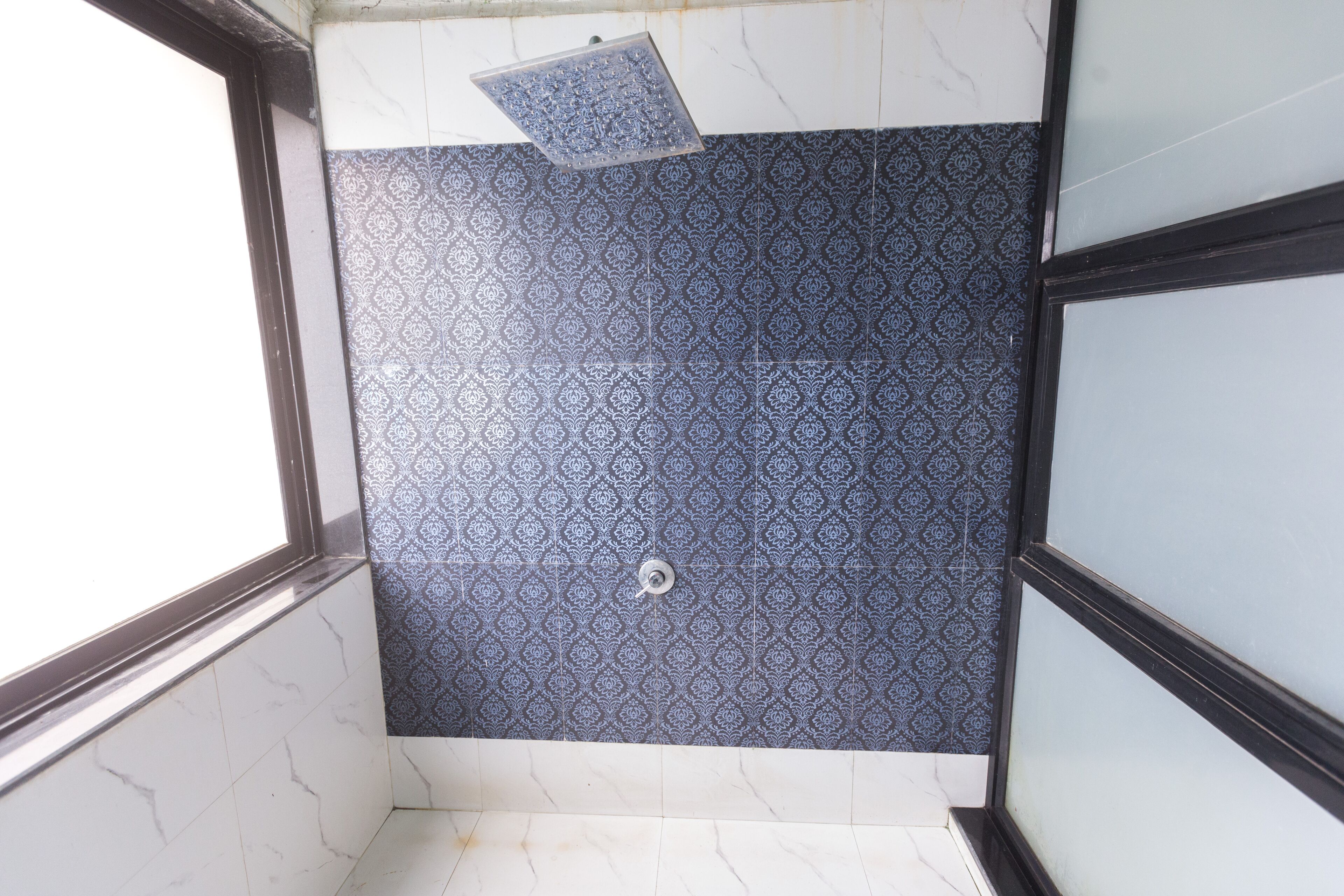 Casa de banho com azulejos estampados, zona de duche e janela.