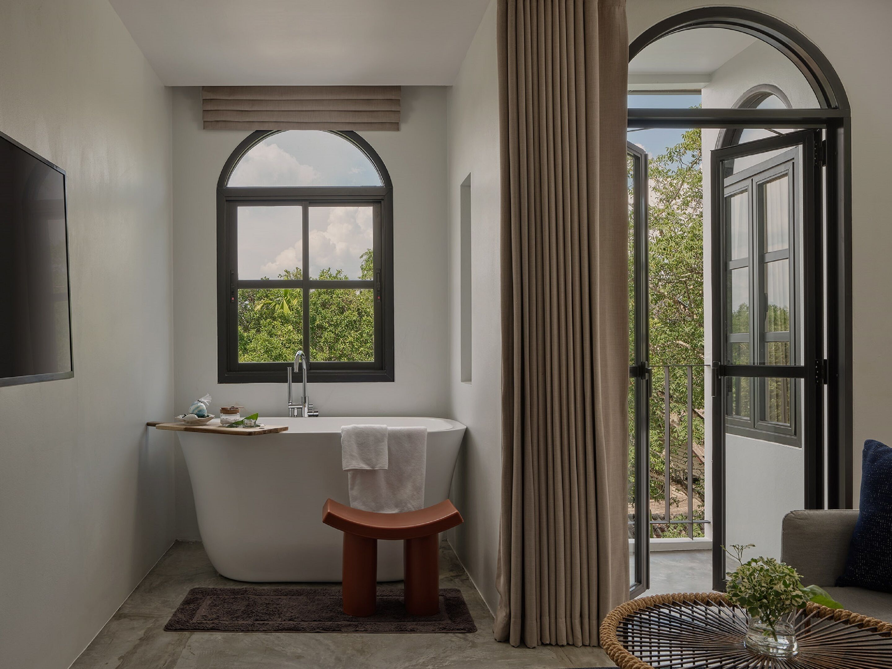 Um banheiro moderno com uma banheira independente, uma janela com vista para vegetação e uma porta que dá para área externa.