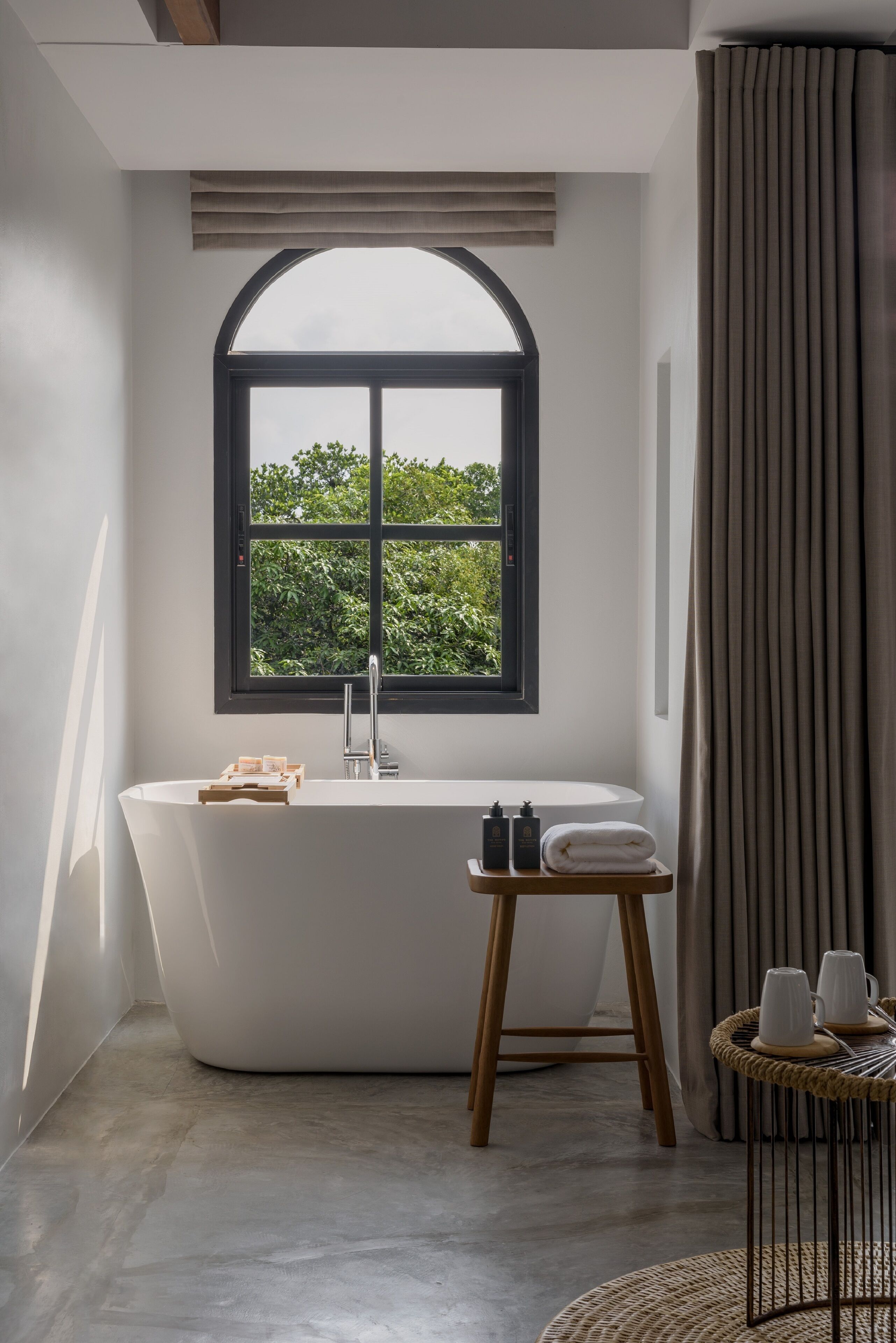Um banheiro moderno com uma banheira livre, uma janela com vista para o verde, um porta-toalhas e um banquinho.